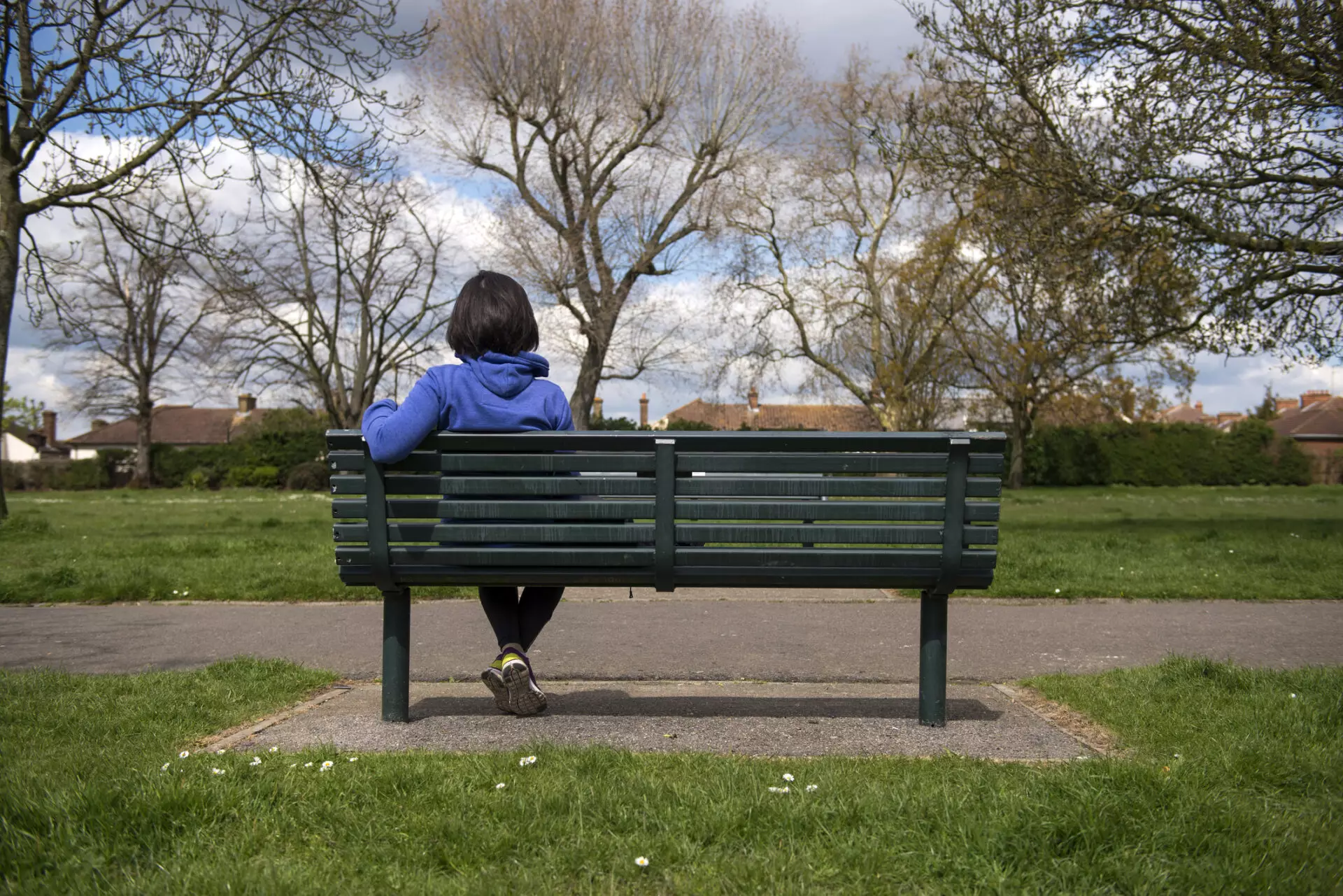 ADHD ženska sedi na klopi s hrbtom obrnjena in gleda v park in razmišlja