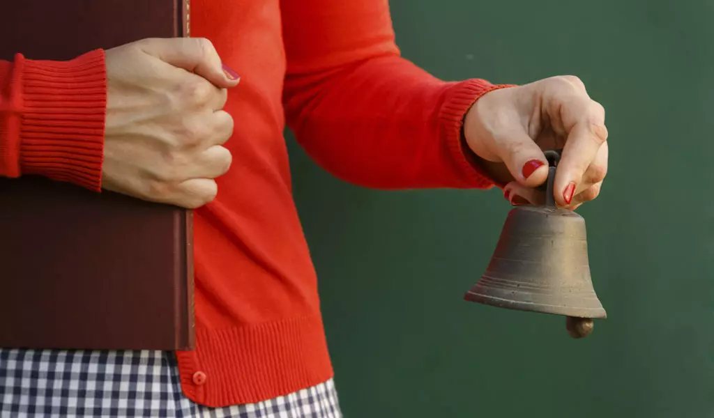 Lærer på skolen ringer med klokken og holder en bog