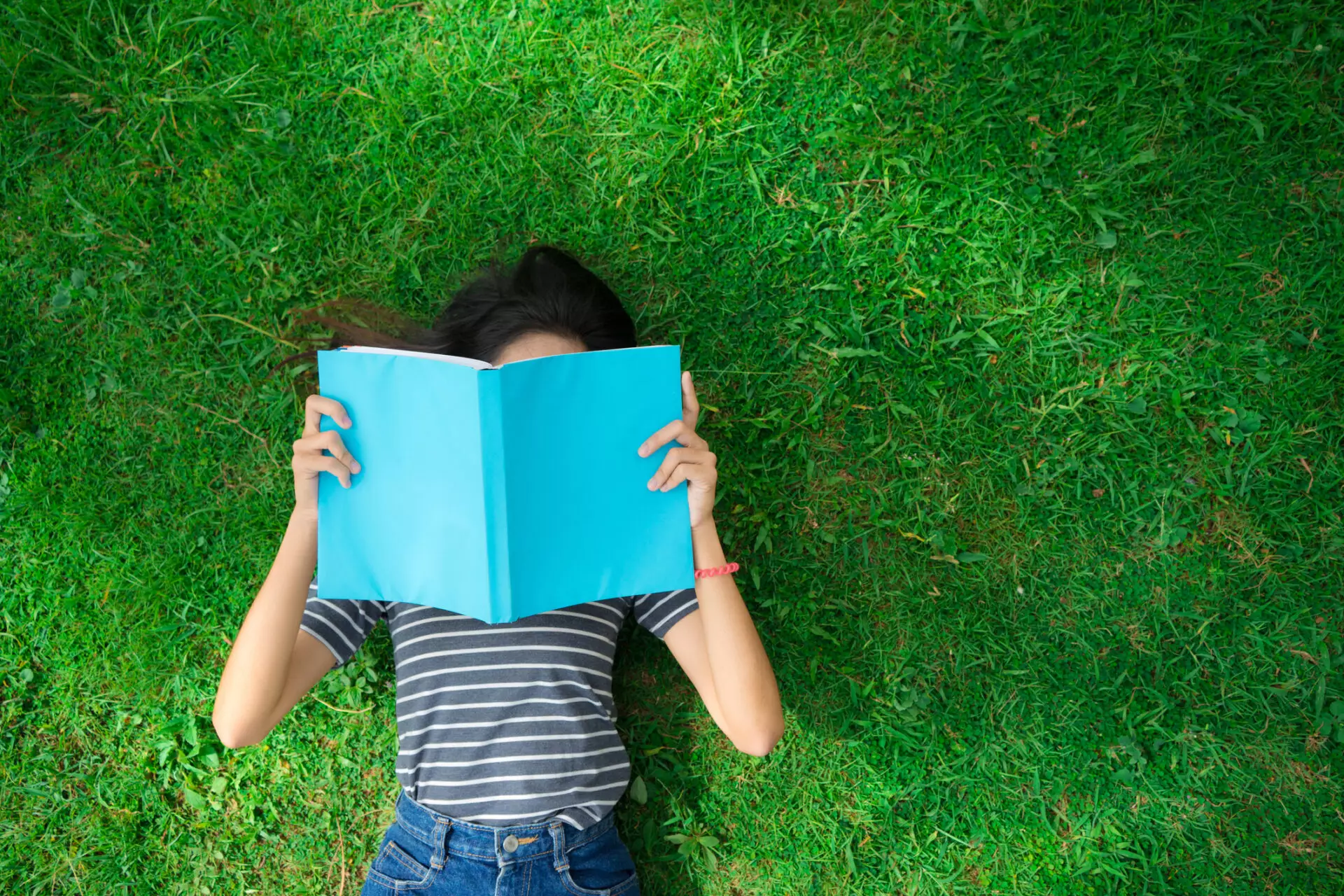 Азиска млада девојка чита книга на горниот поглед на паркот