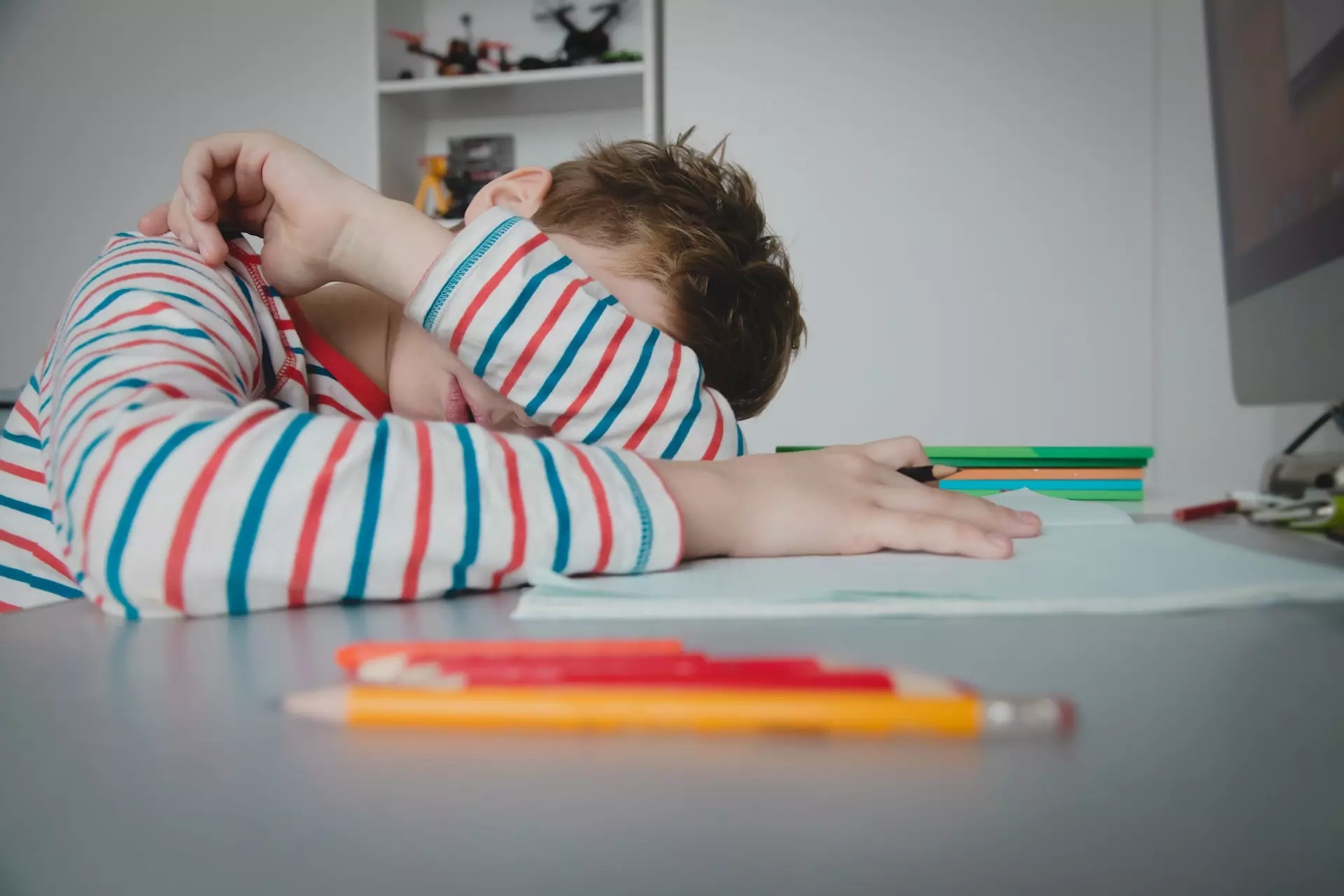 Bambino che posa la testa sulla scrivania con l'avambraccio sugli occhi, stanco dell'apprendimento a distanza.