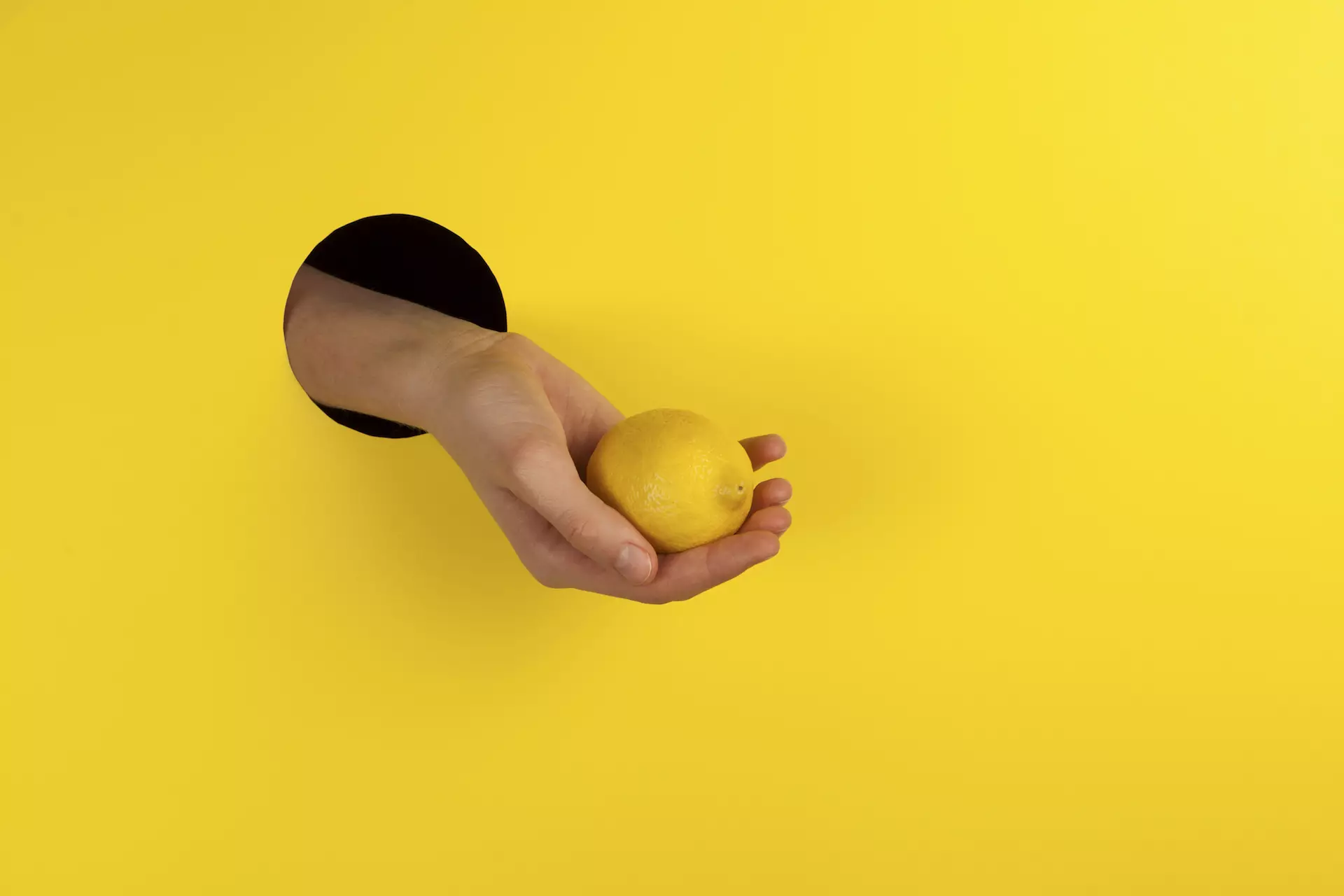 Mão em um buraco em um fundo amarelo e oferece limão.