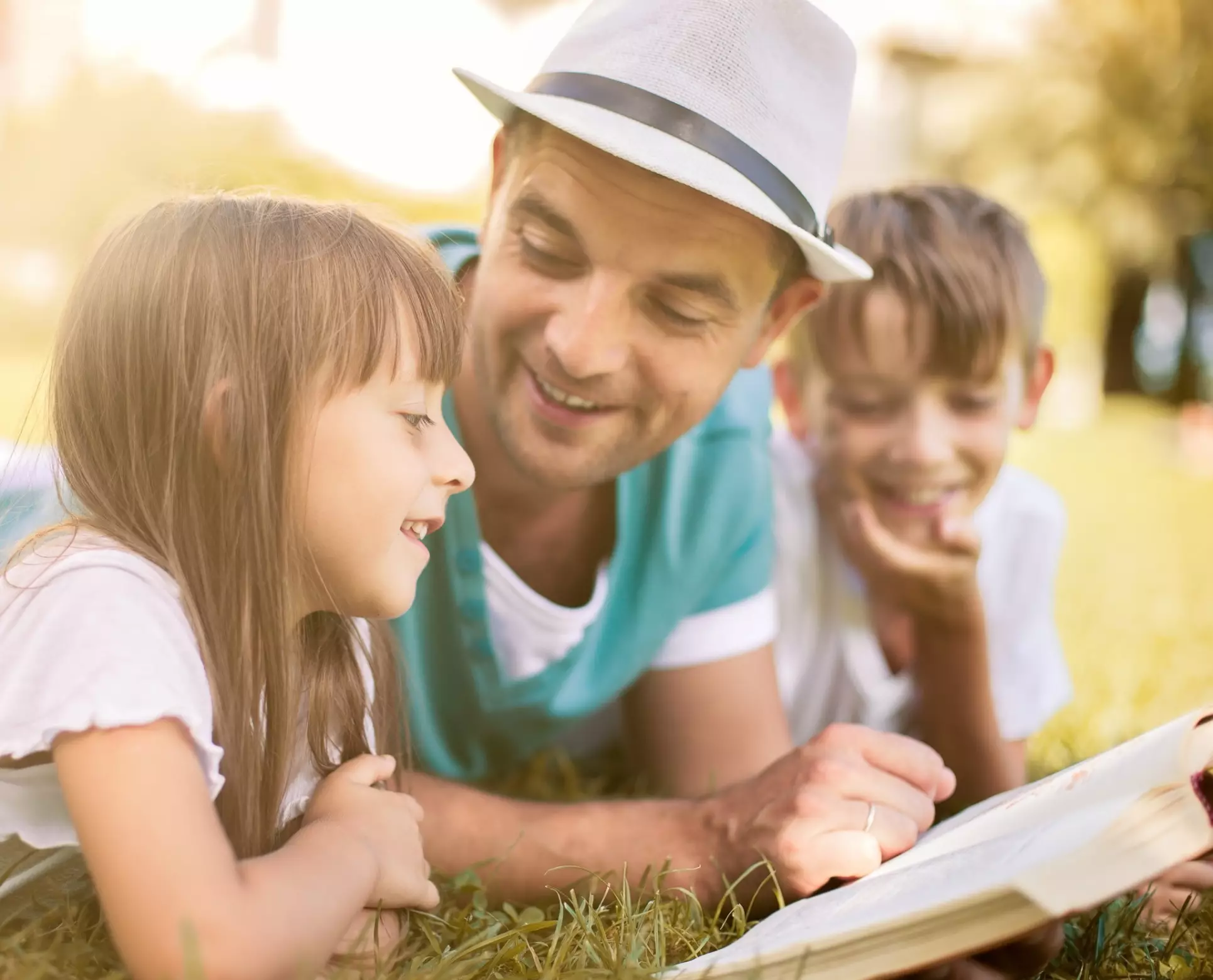 Um pai lê com seus dois filhos no parque. Passar tempo de qualidade juntos é uma estratégia de como ser um pai melhor.