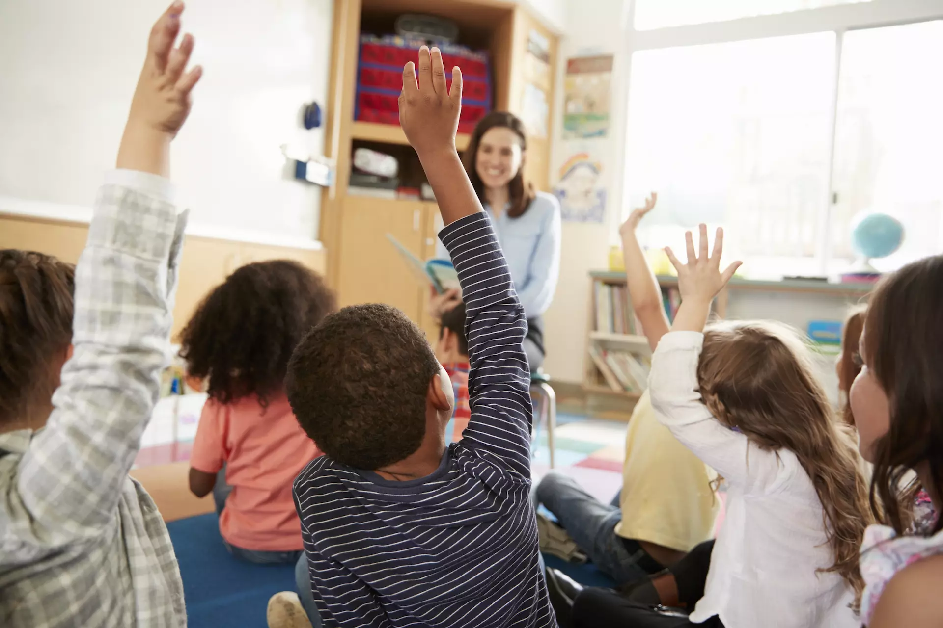 Дети начальной школы поднимают руки к учителю, вид сзади
