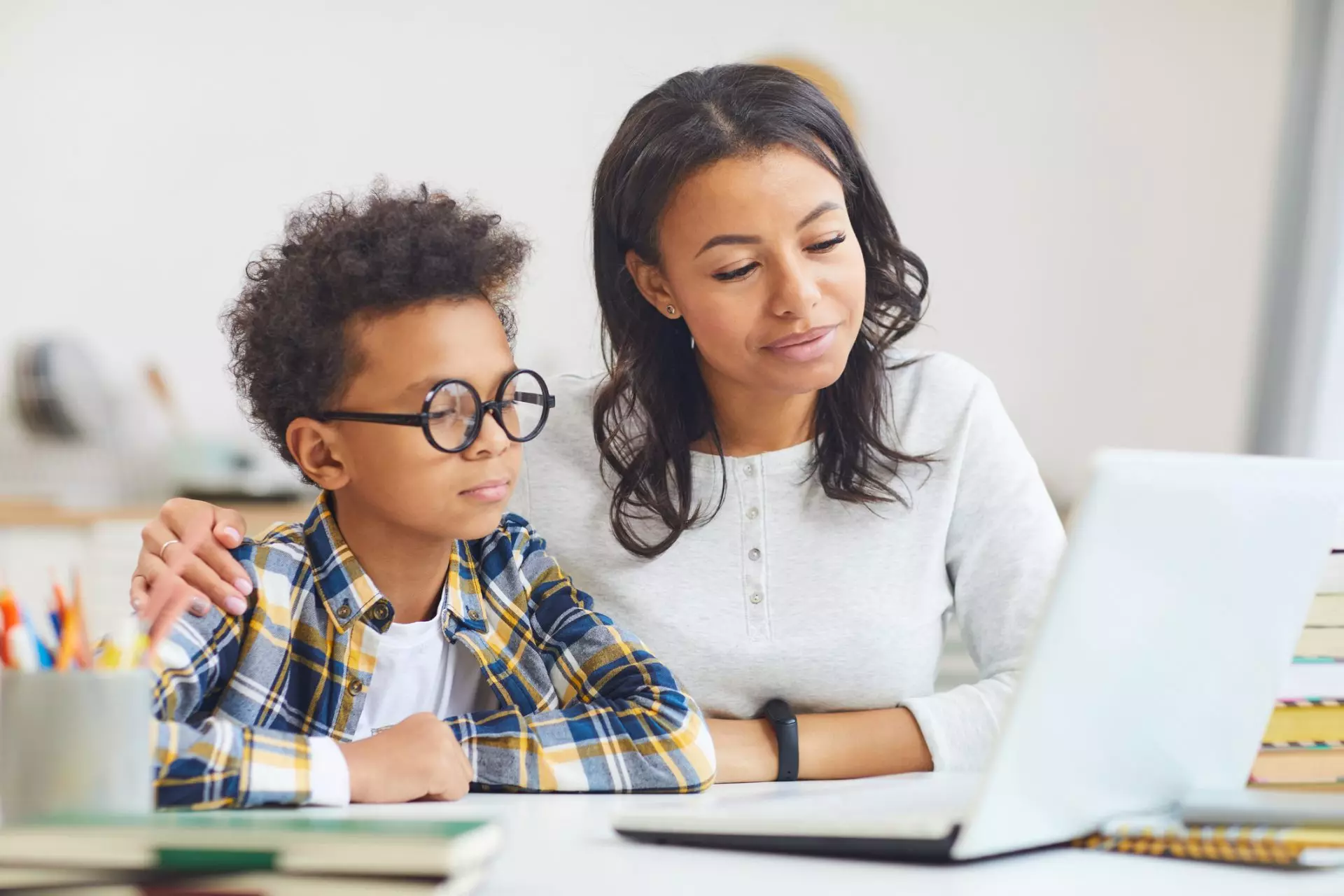 Potret budak lelaki Afrika comel memakai cermin mata besar sambil menggunakan komputer riba dengan ibu, homeschooling dan konsep pendidikan jauh