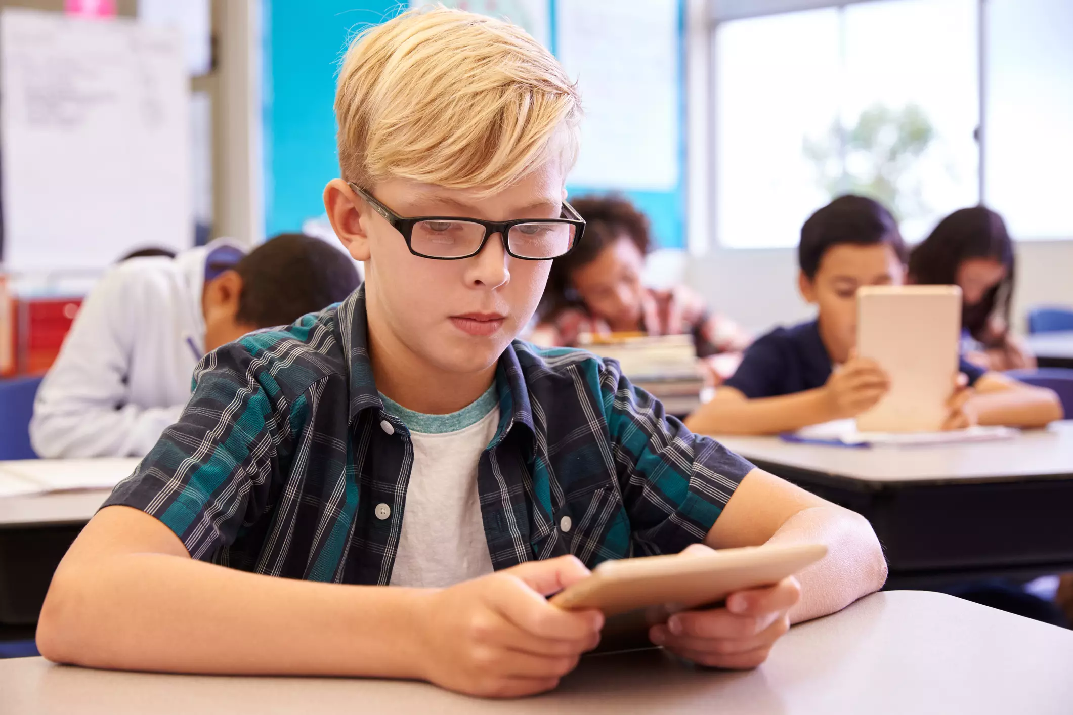 Băiat cu ADHD purtând ochelari folosind tableta în clasa de școală elementară