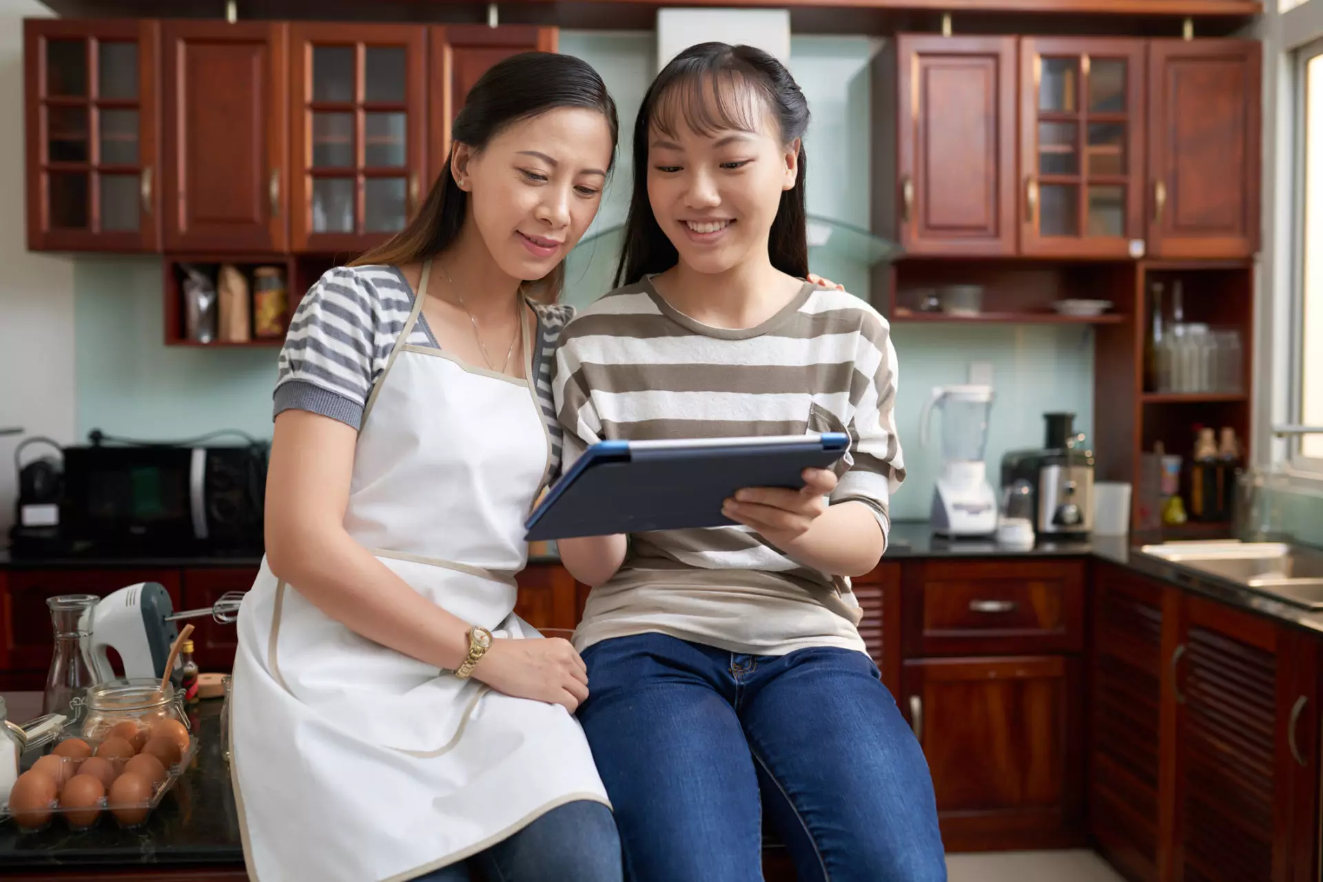 Hymyilevä vietnamilainen äiti ja tytär lukevat uuden ruokalajin reseptiä tablettitietokoneella